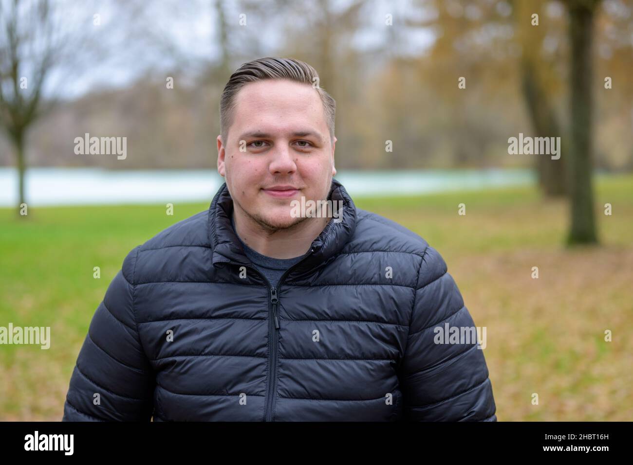 Happy young man grinning at the camera as he stands outdoors in a park ...