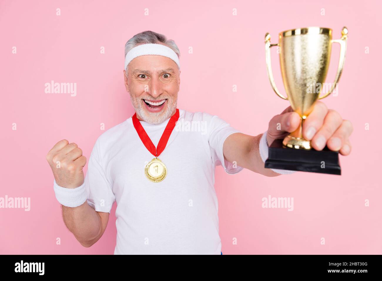 Photo portrait of senior man in headband smiling showing prize ...