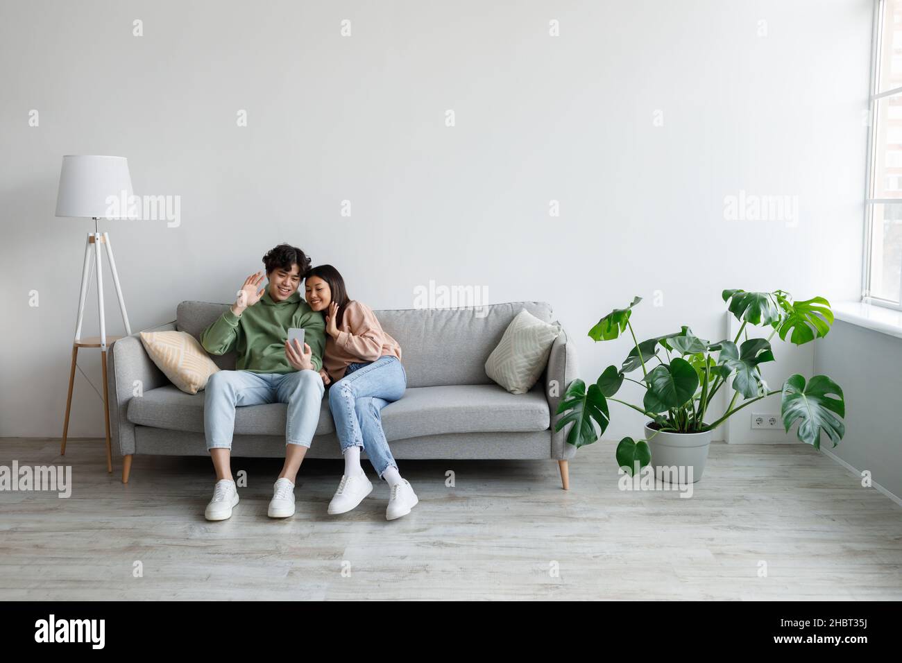 Cheerful young Asian couple waving at smartphone camera, chatting ...