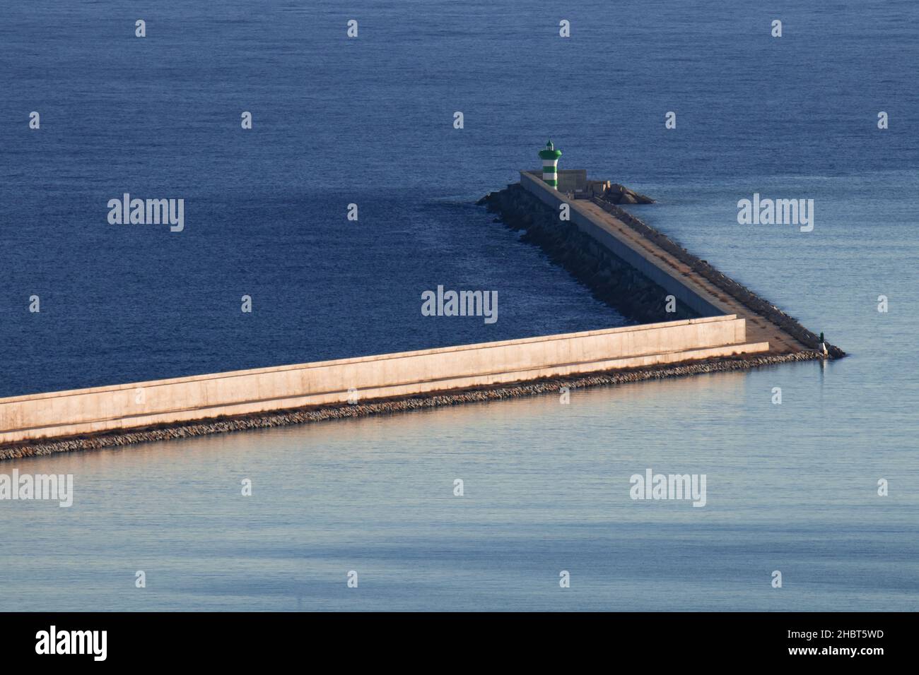 A long stone pier over the sea water surface with a lighthouse in the ...