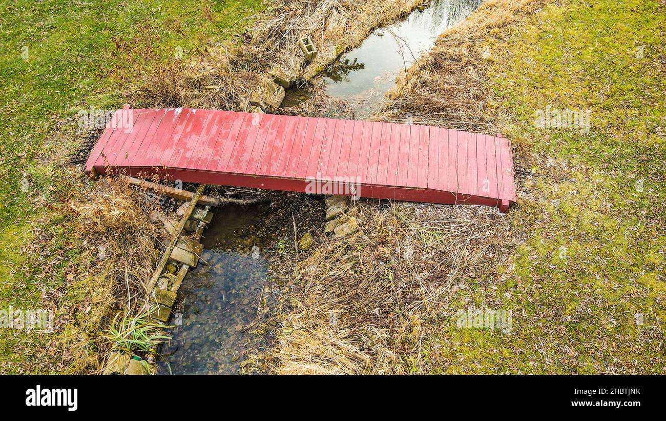 Rural red footbridge over small stream with green grass and water Stock ...