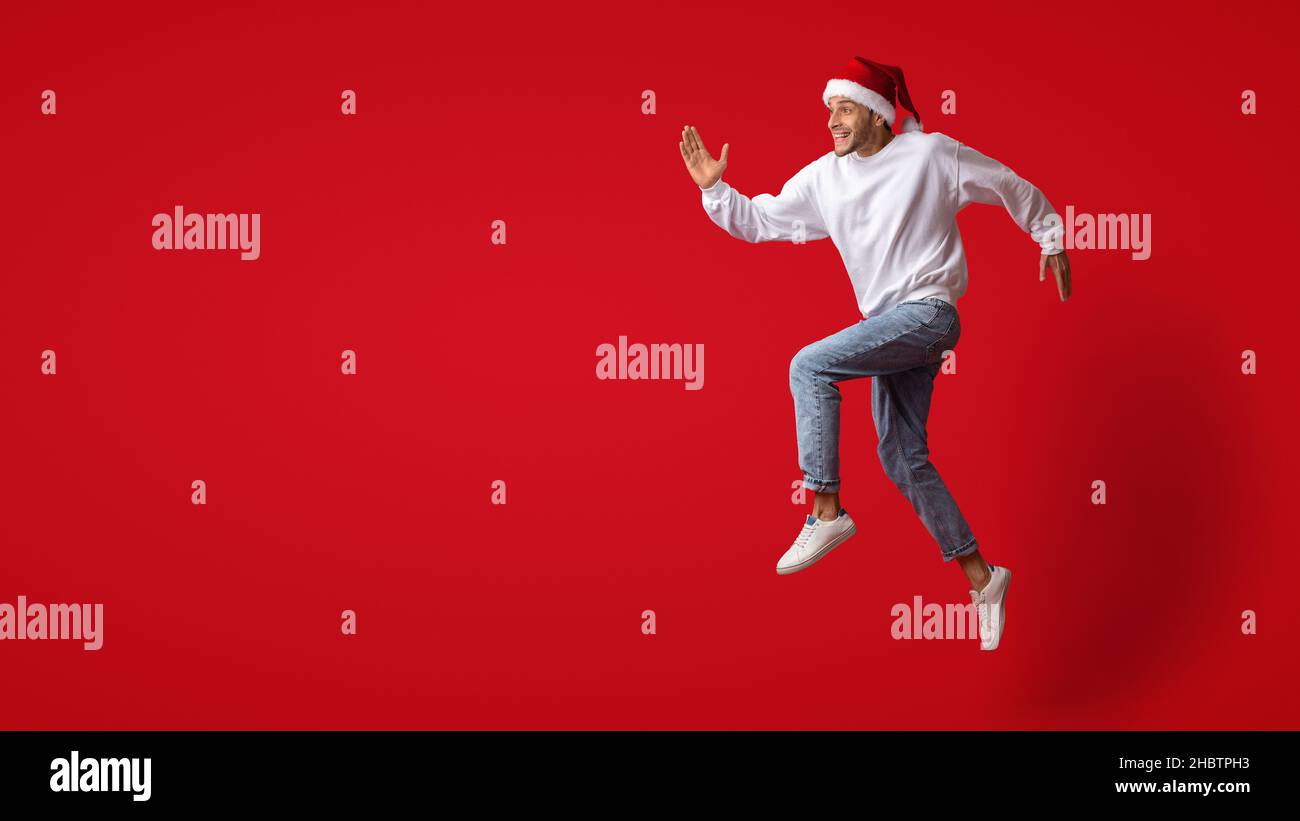 Christmas Rush. Excited Young Man In Santa Hat Jumping On Red ...
