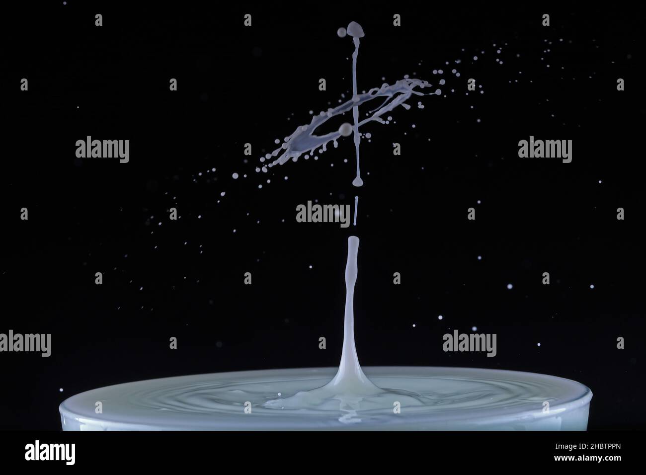 A drop of milk falls into a cup isolated with a black background Stock ...