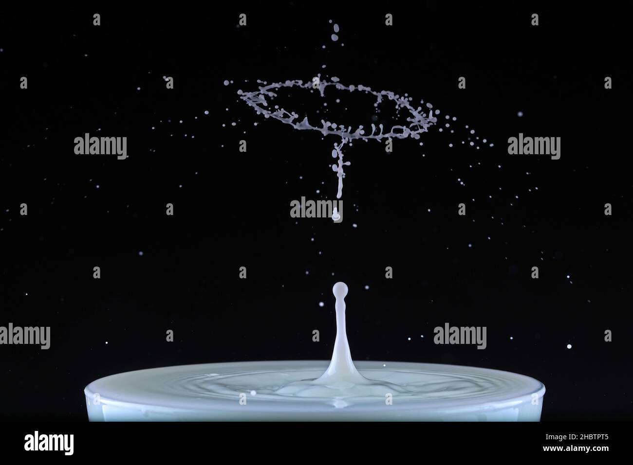 A drop of milk falls into a cup isolated with a black background Stock ...