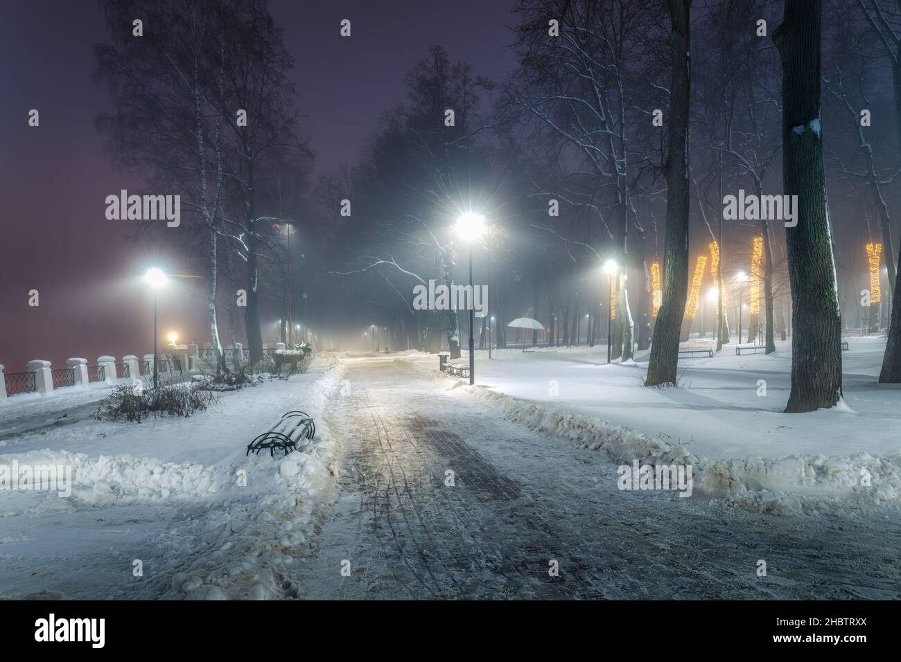 First snow in a winter night park with trees, glowing lanterns and ...