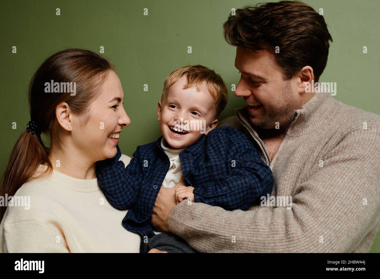 Cozy portrait of loving parents holding little boy and laughing candid ...