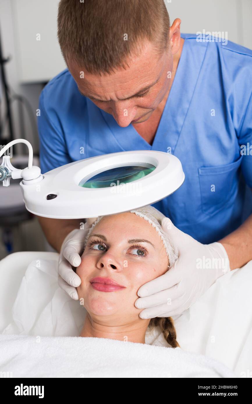 Man doctor is analysing skin on face of female patient before the ...
