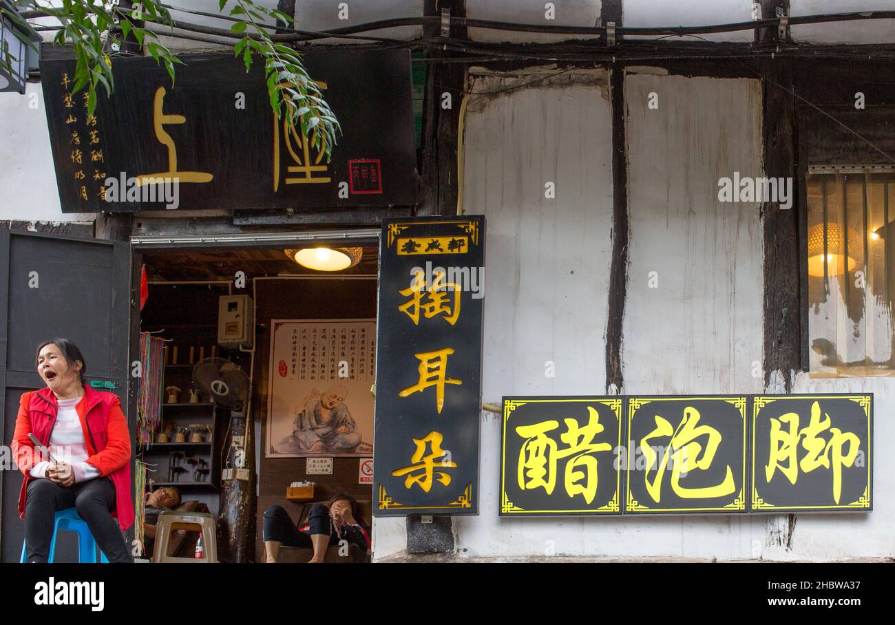 Middle aged woman yawning outside a place to relax. Chongqing. Popular ...