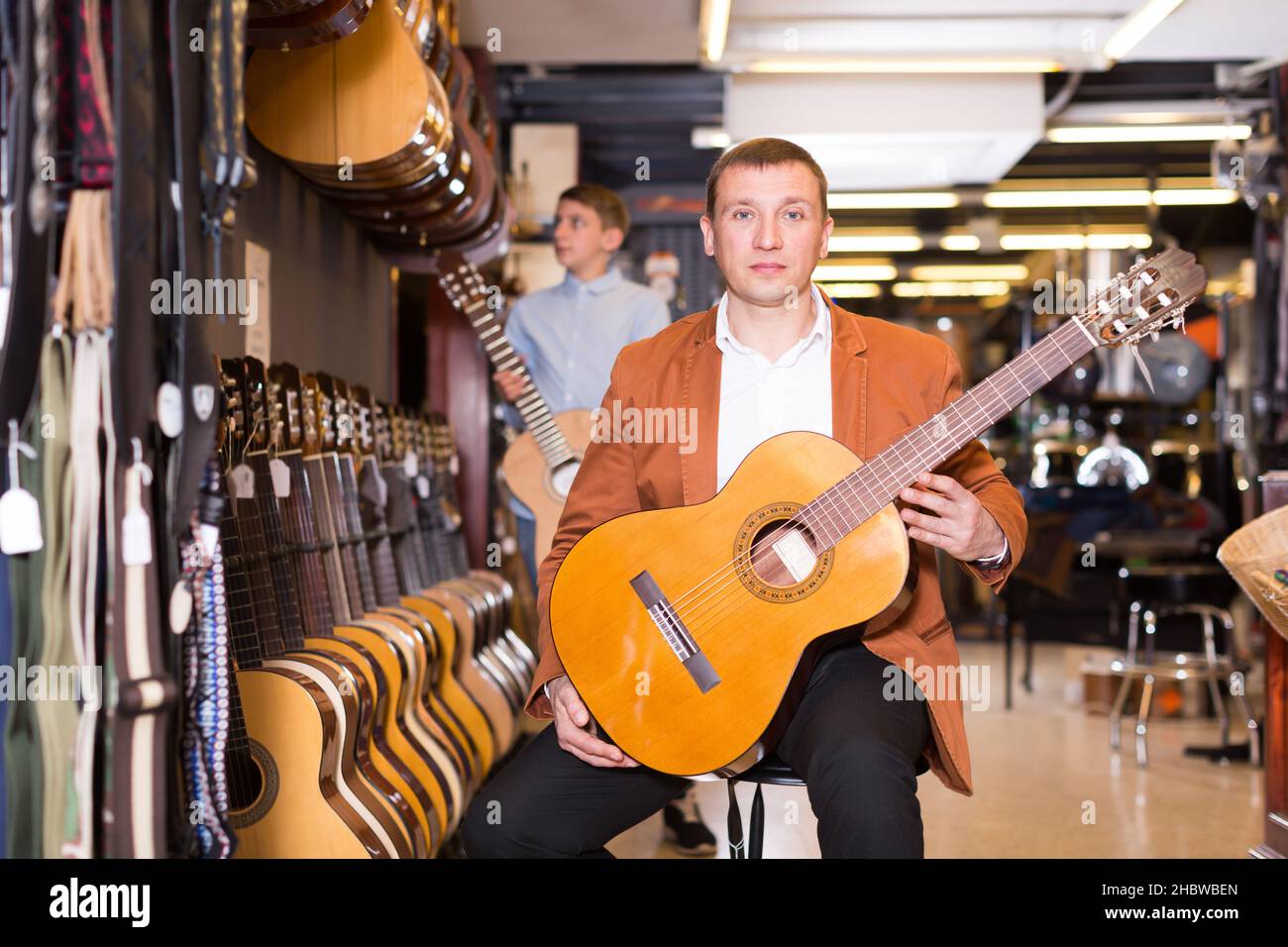 Glad male seller showing guitar to boy client Stock Photo - Alamy