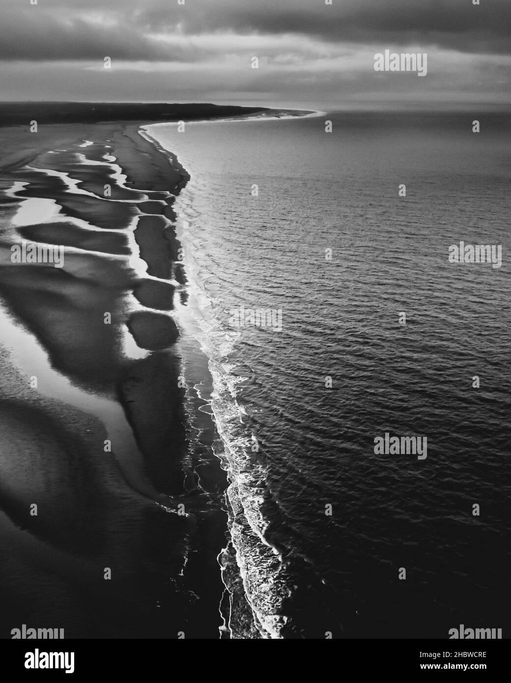 A vertical grayscale shot of a beach with beautiful sea waves under a ...