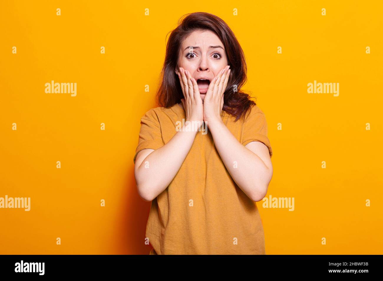 Portrait of terrified person holding hands on face to pose on camera. Scared woman screaming and ...