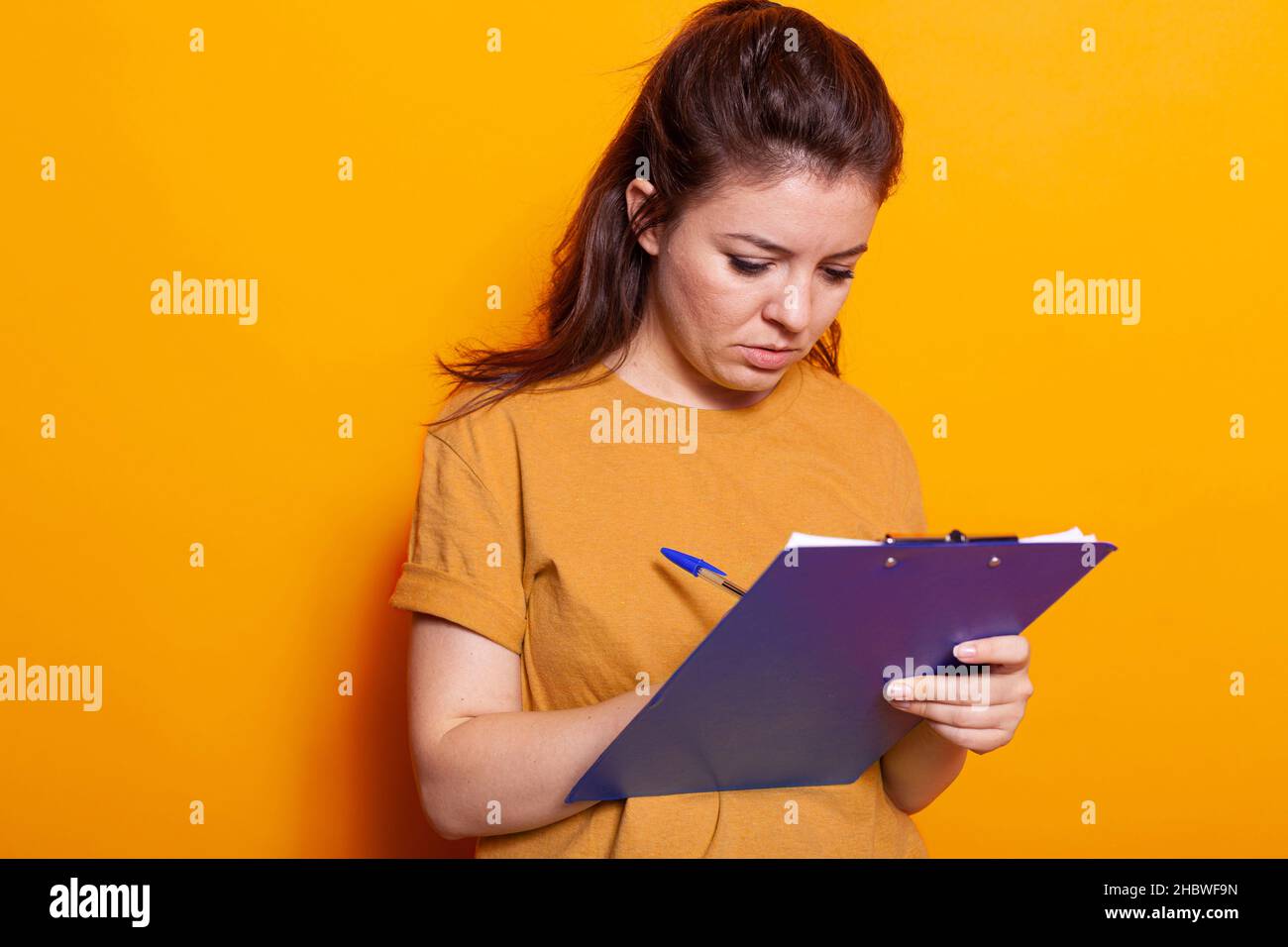 Young woman taking notes on textbook papers with pen in studio ...