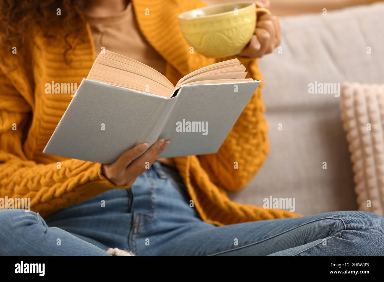 Young woman with cup of hot tea reading book on sofa at home Stock ...