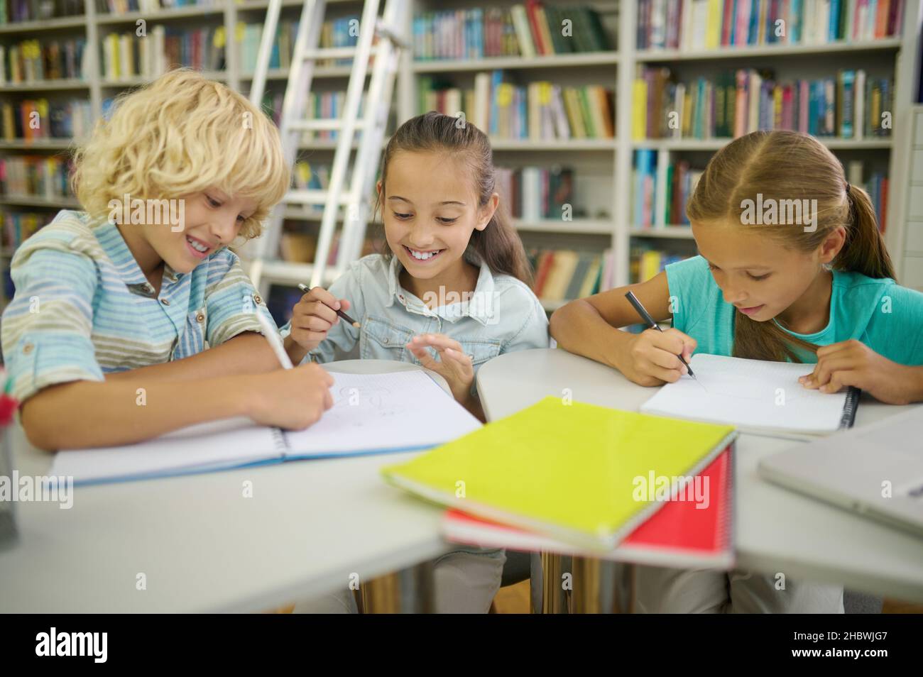 Boy and two girls writing and painting in library Stock Photo - Alamy