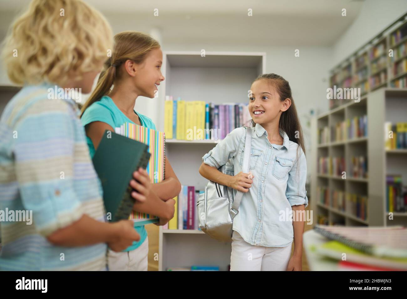 Two girls and boy standing talking in library Stock Photo - Alamy