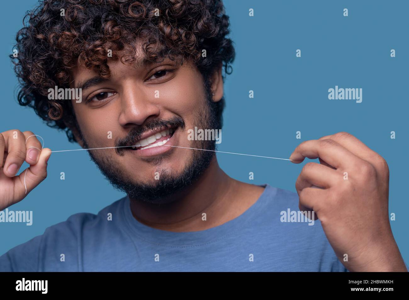 Smiling guy with curly hair flossing his teeth Stock Photo - Alamy