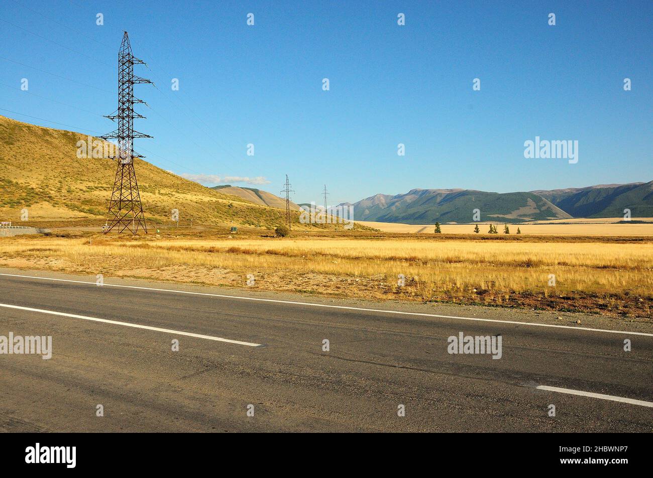 Tall metal poles of power lines crossing the road go through the desert ...