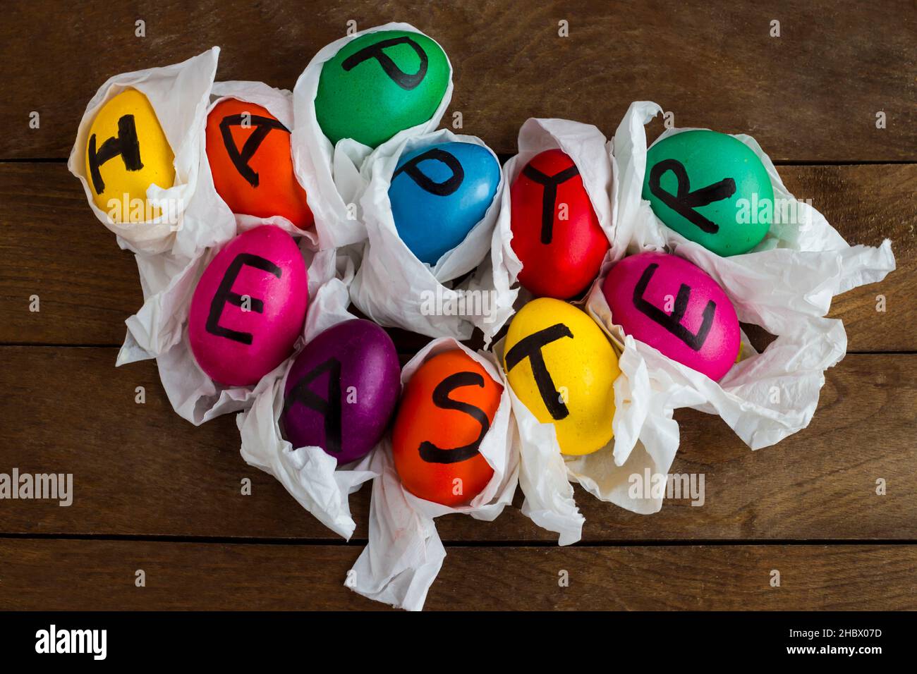 Colorful Easter Eggs with white papers on the wooden table.Writing by ...