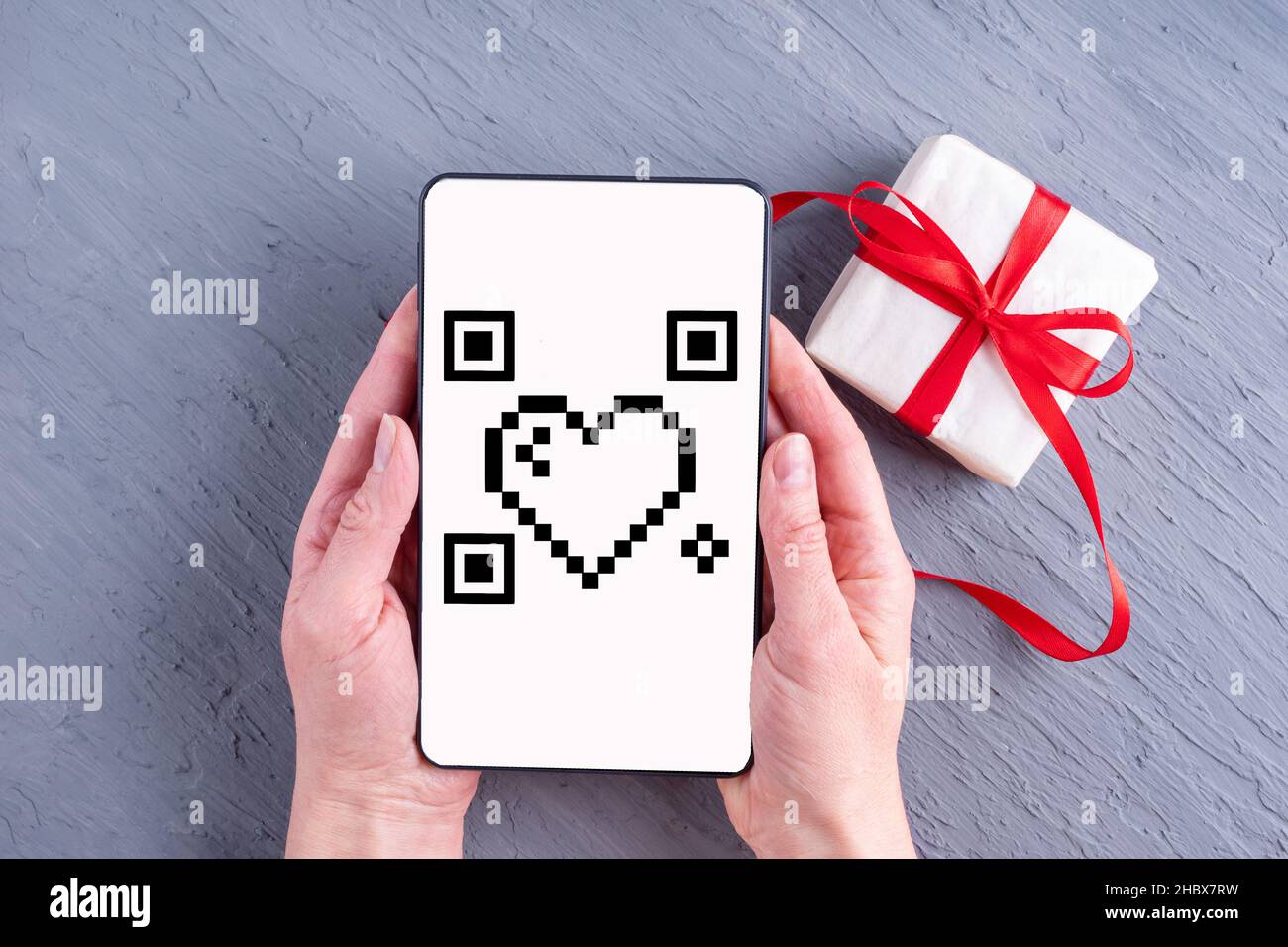 Hands holding mobile phone with white screen with heart shaped qr code ...