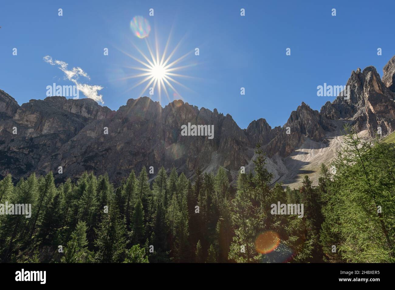Sun with rays illuminating the ridge of the Dolomites and fresh green ...