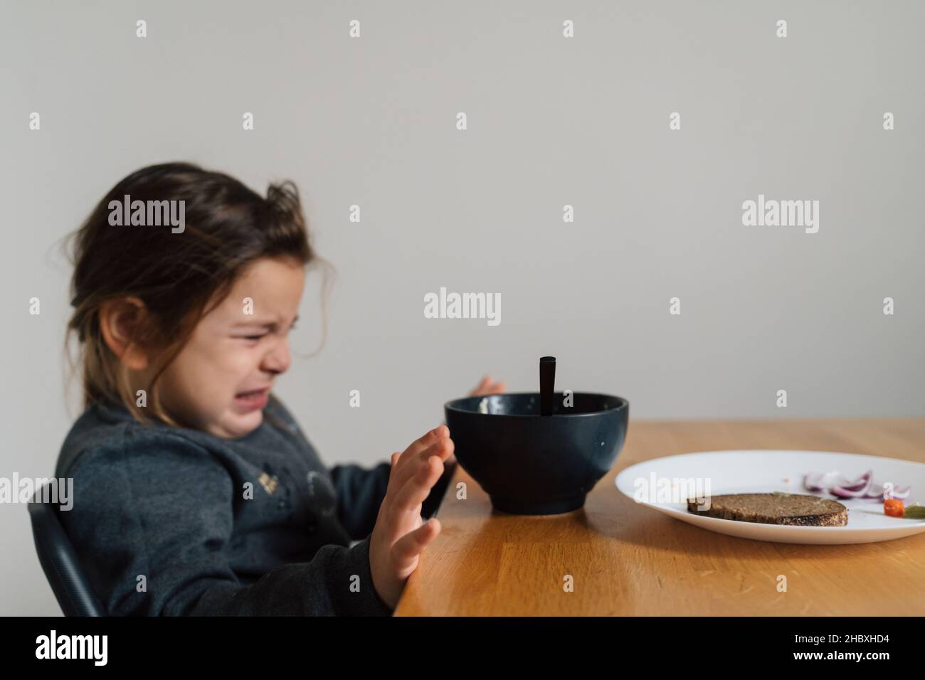 Unhappy child girl eats soup from black bowl with bread and onion ...