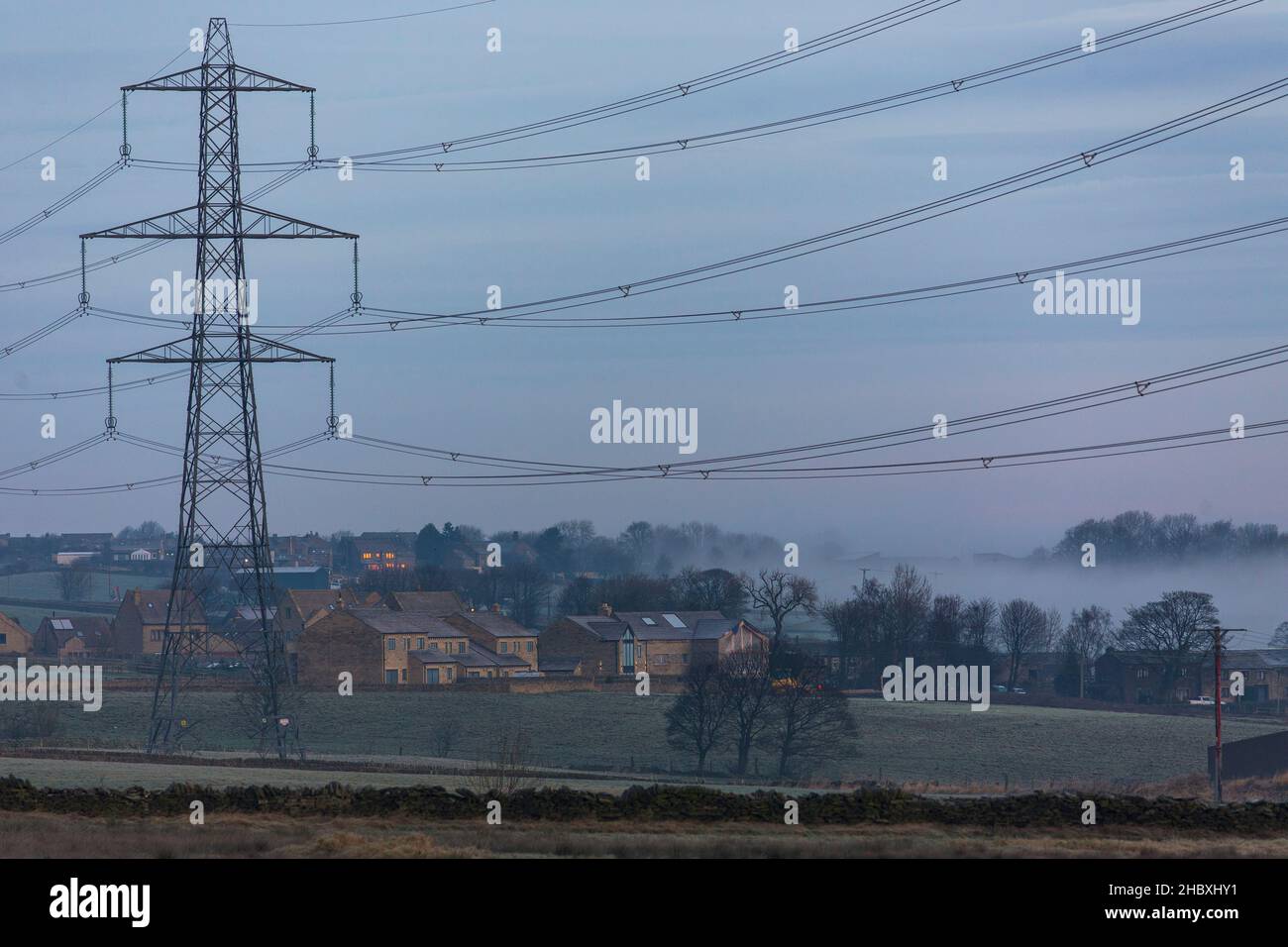 Electricity pylons on a cold misty morning at dawn cross the Pennine ...