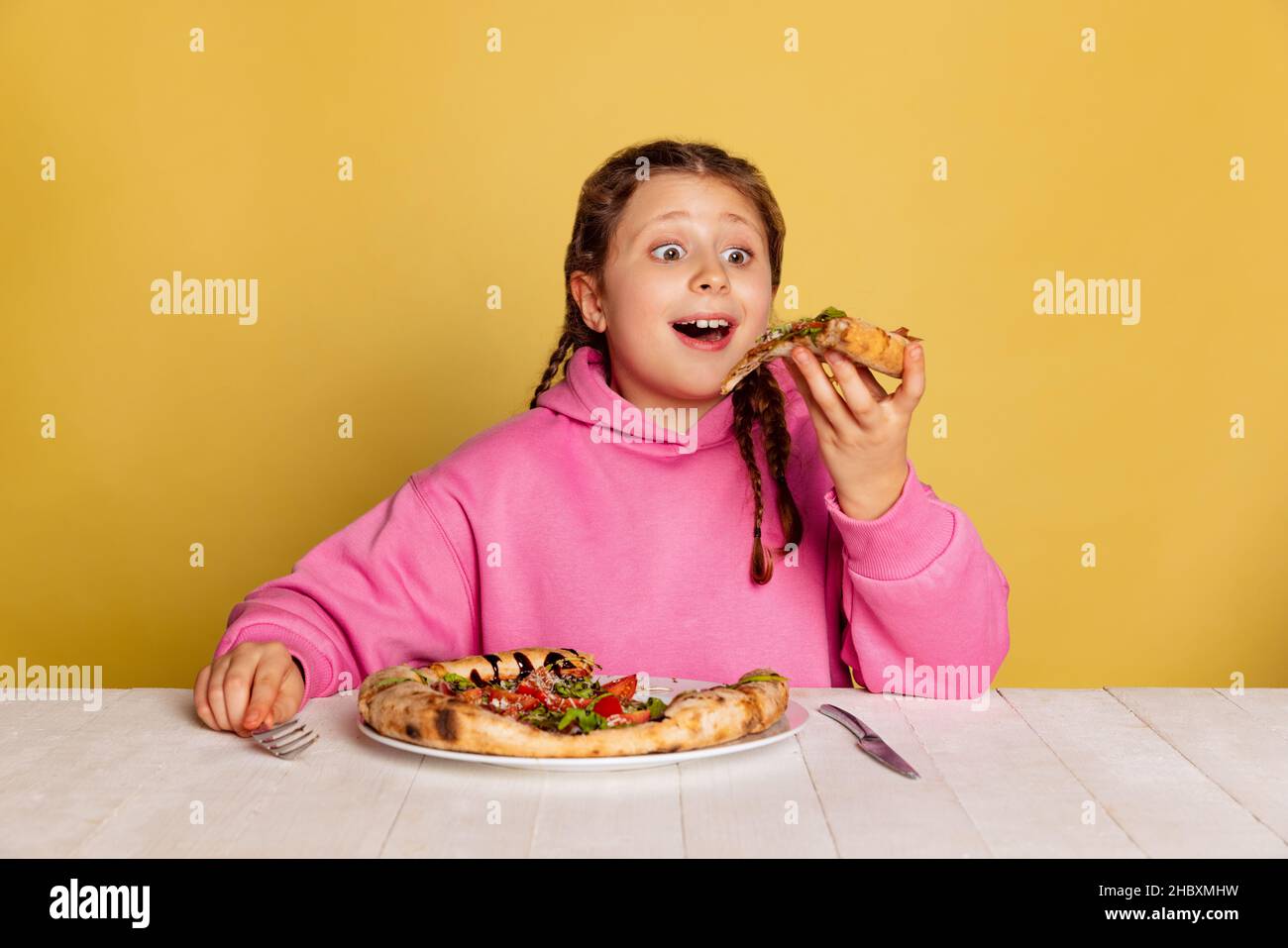 Studio shot of little cute girl sitting and tasting delicious Italian ...