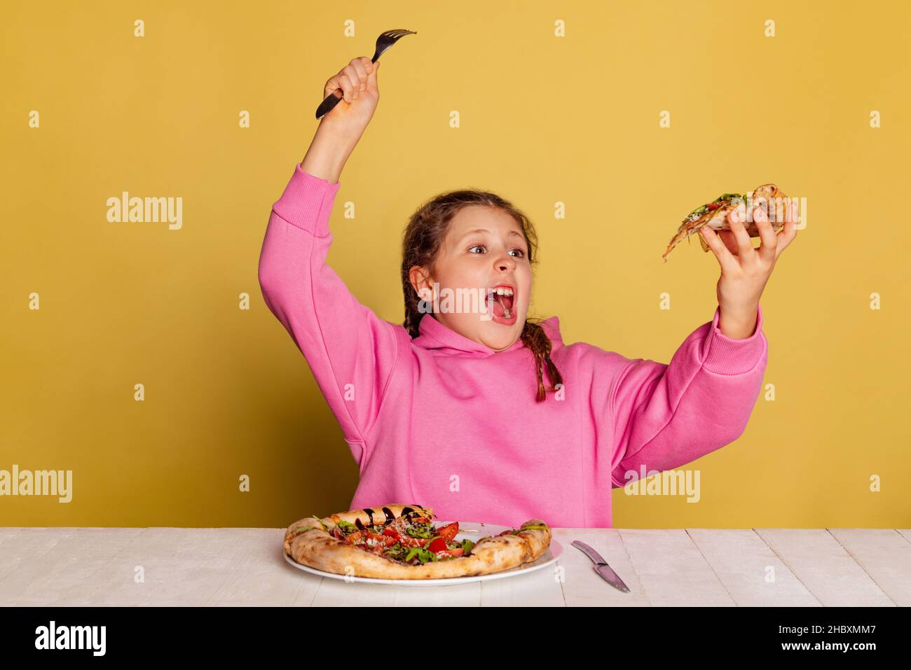 Studio shot of little cute girl sitting and tasting delicious Italian ...