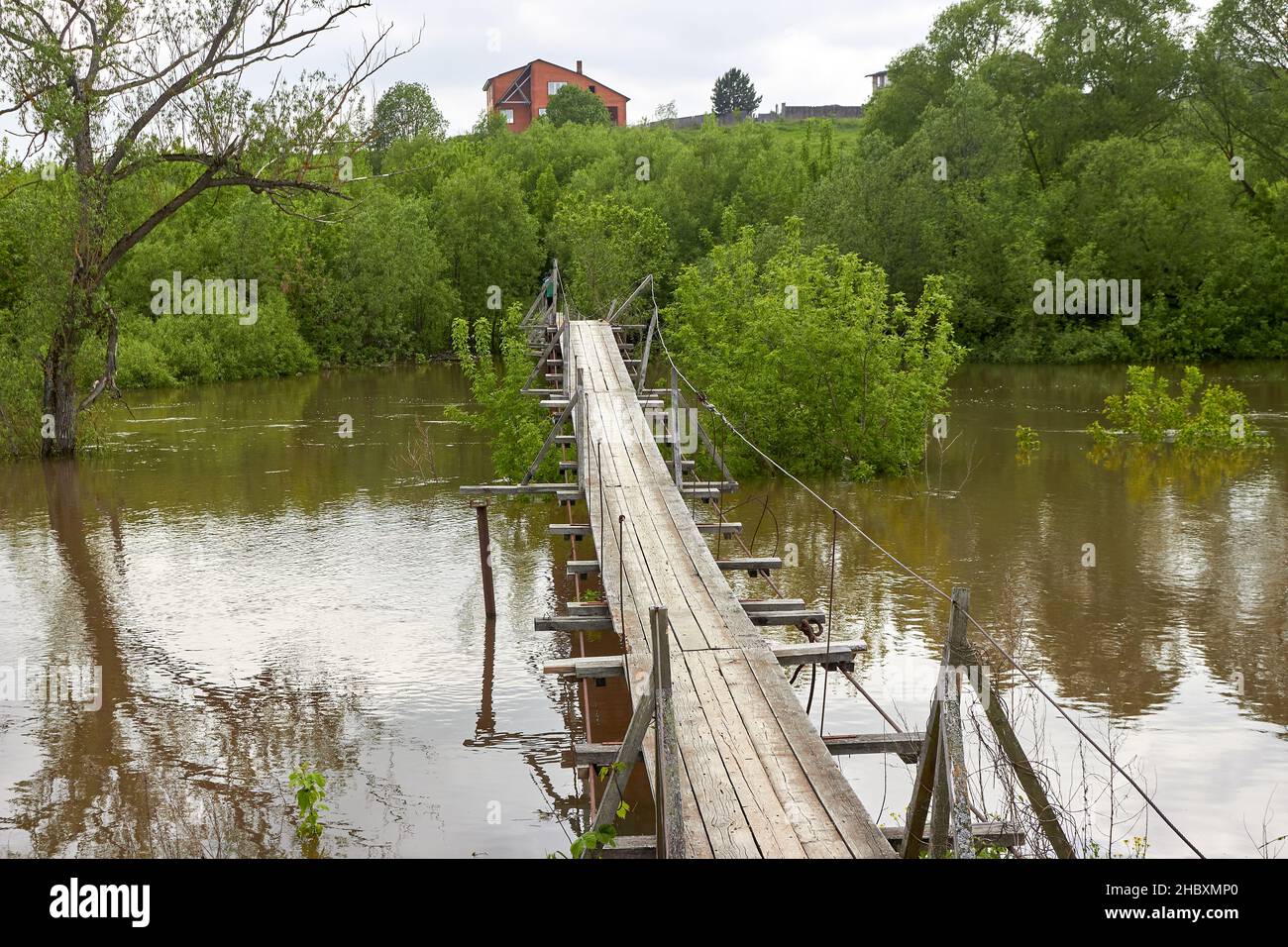 Rustic suspension footbridge across the river during flood after rains ...