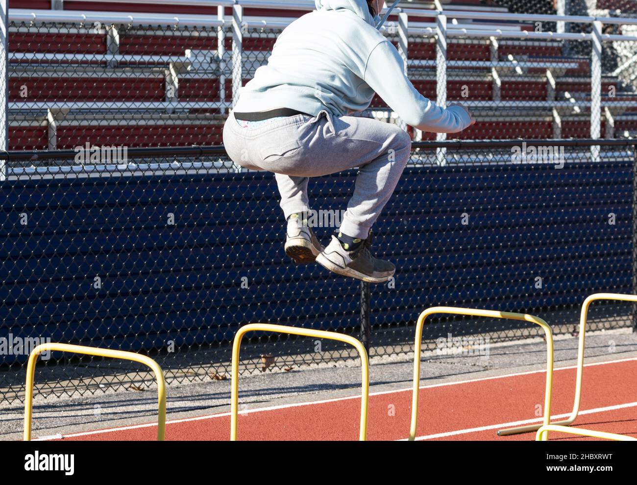 High school boy jumping over two foot tall yellow hurdles in front of ...