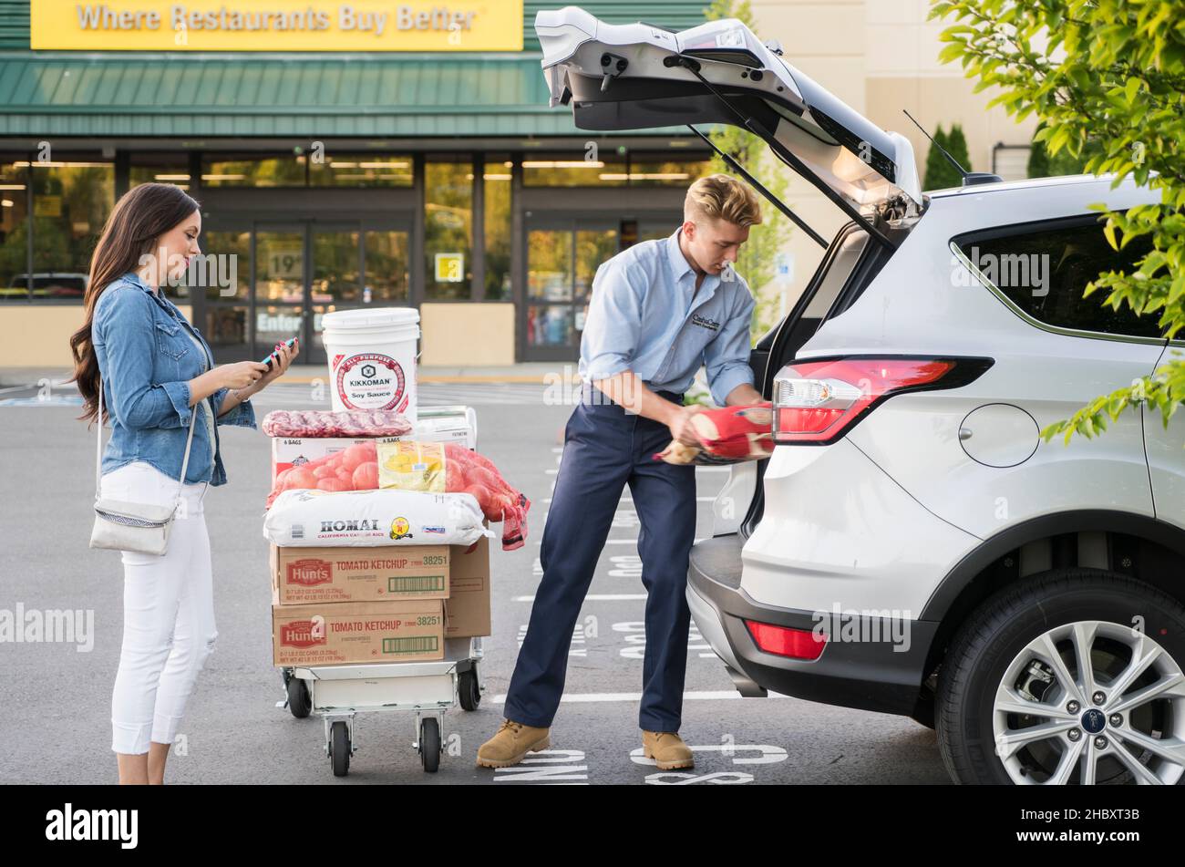 A store employee loading goods and groceries into the trunk of a car ...