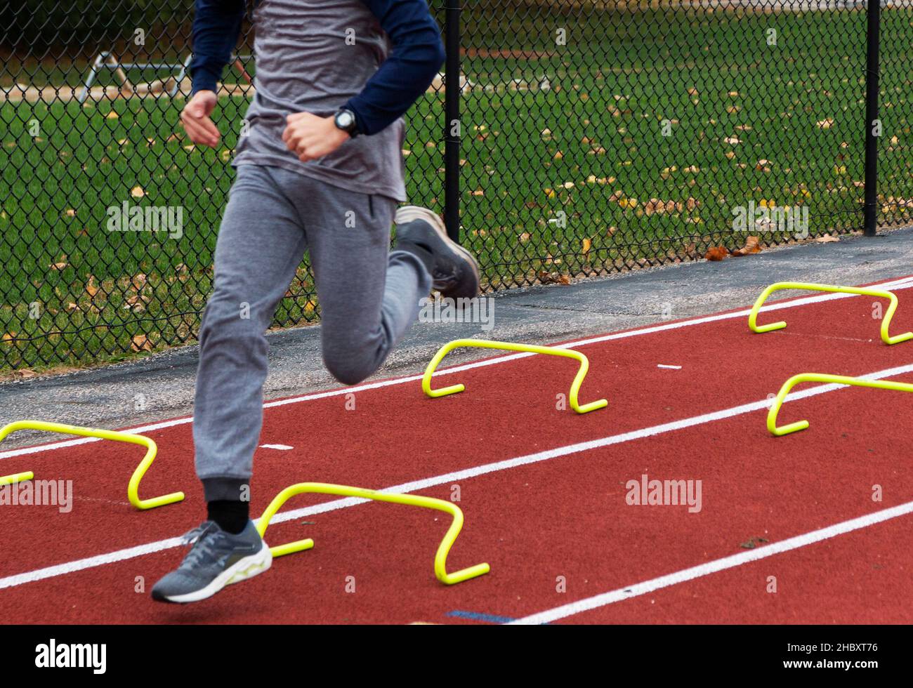 A high school boy is running over small yellow hurdles on a red track ...