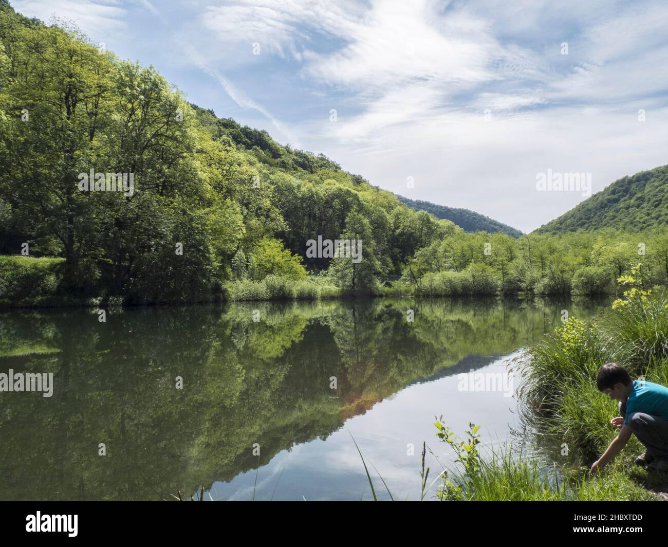 View over flat calm lake water, mountains and woodland, a boy on the ...