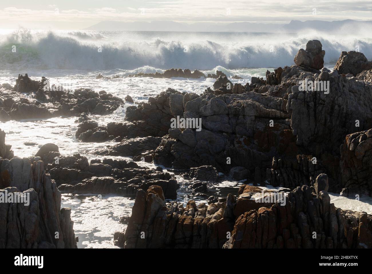 Jagged rocks on the shore at De Kelders, tall waves rolling in and ...