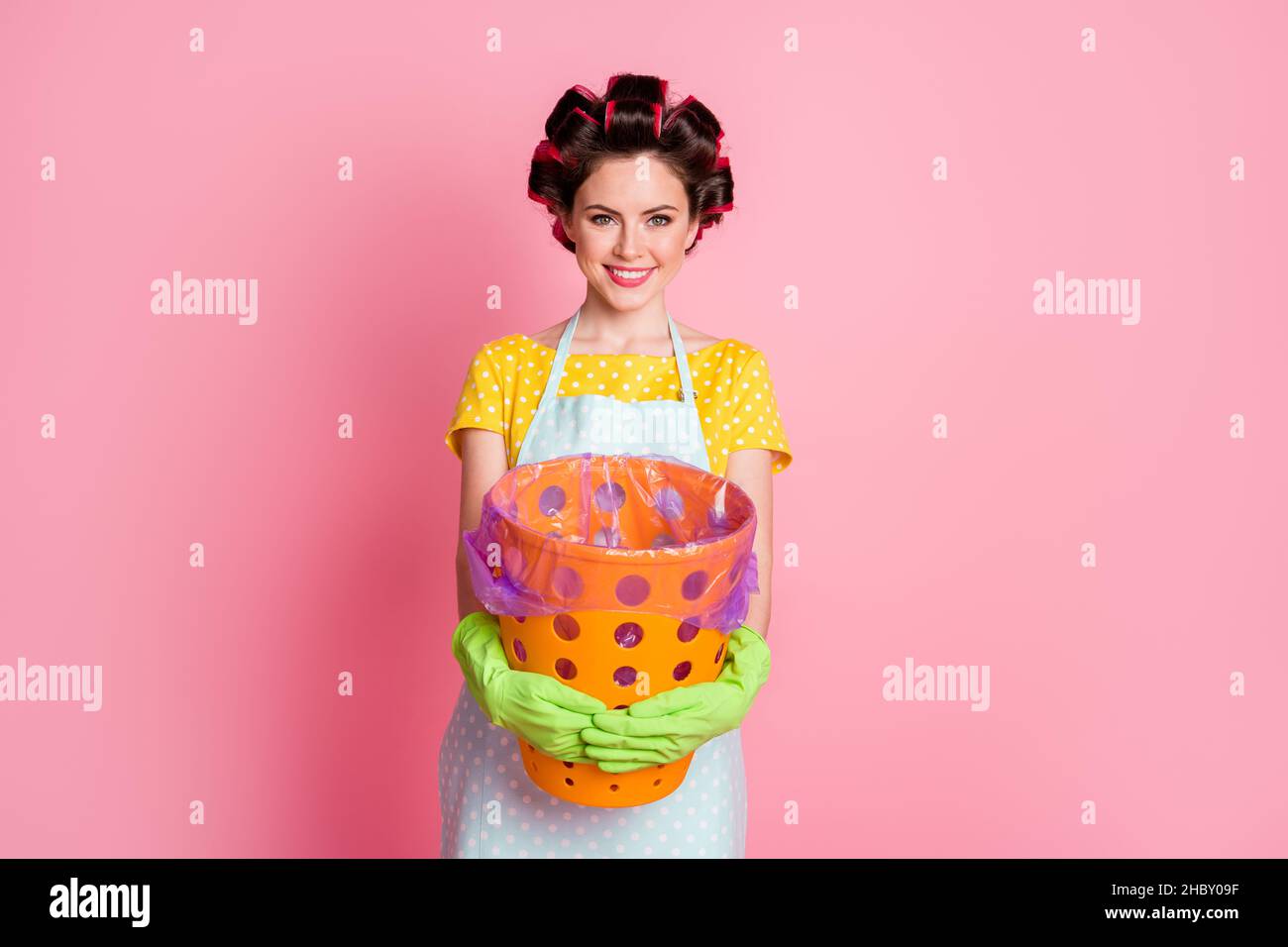 Portrait of pretty cheerful maid homemaker holding in hands trash bin ...