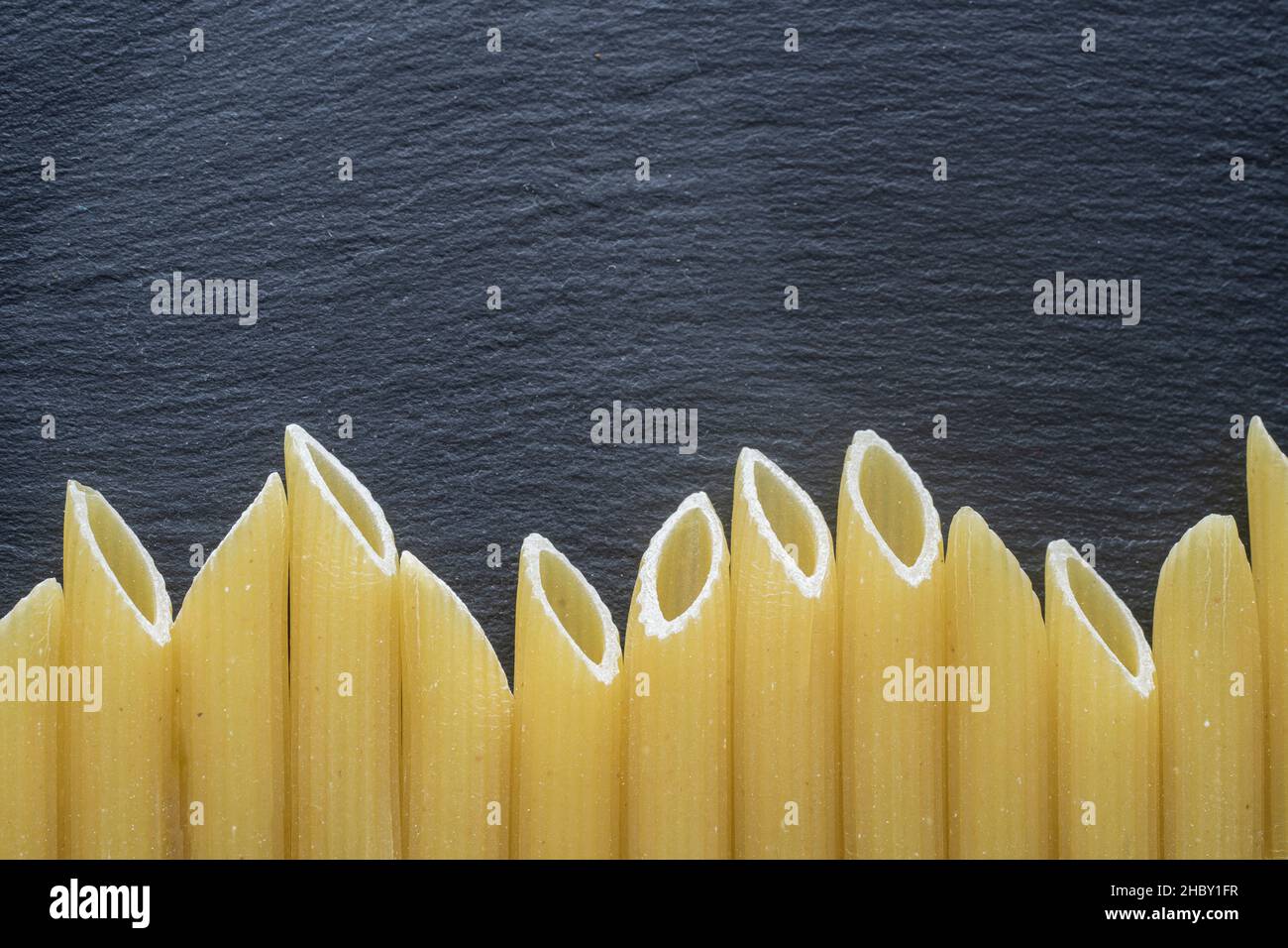 Penne pasta border isolated on a black tile, stone texture Stock Photo ...