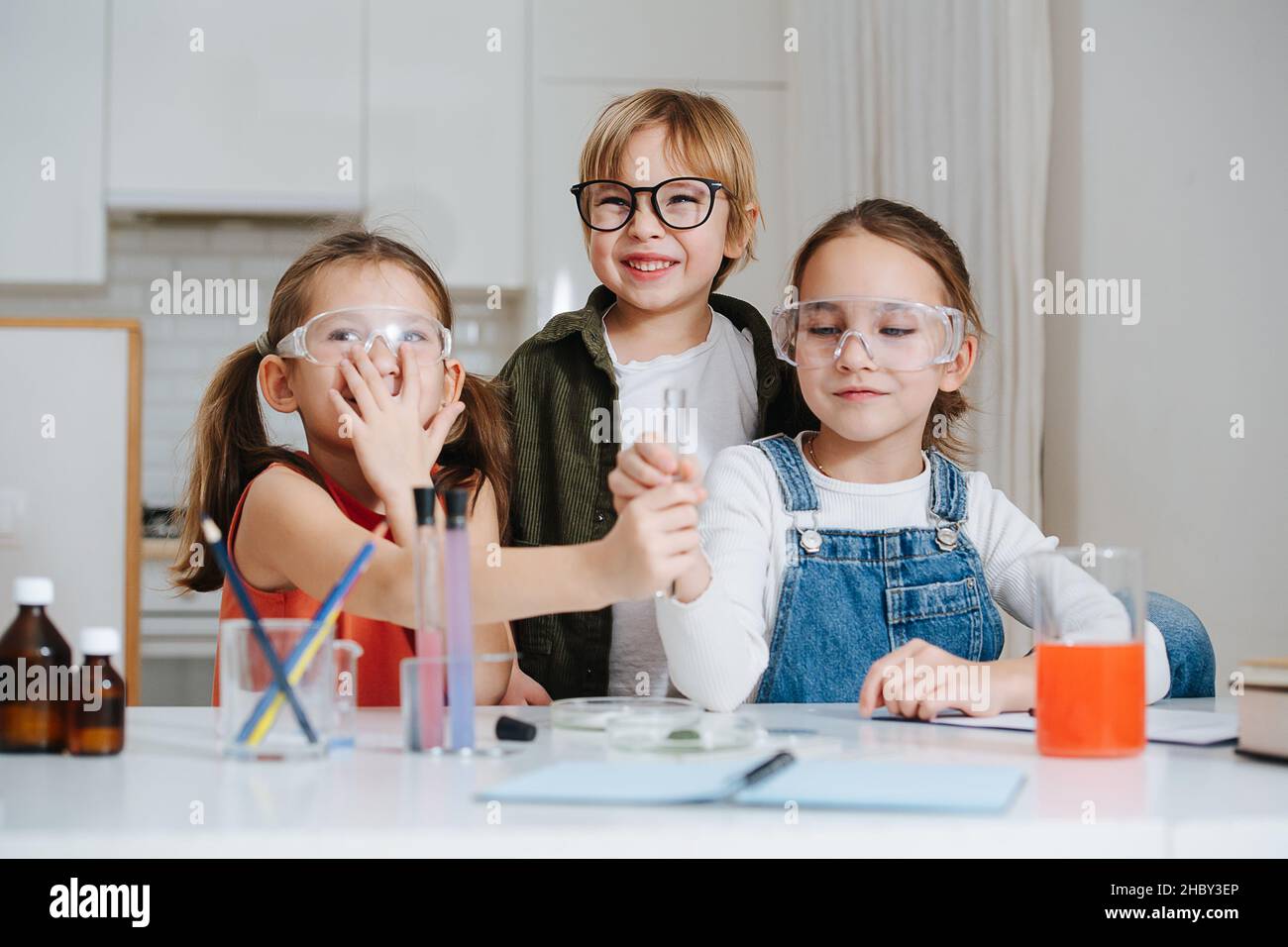 Lively little kids doing home science project, passing a flask. All ...