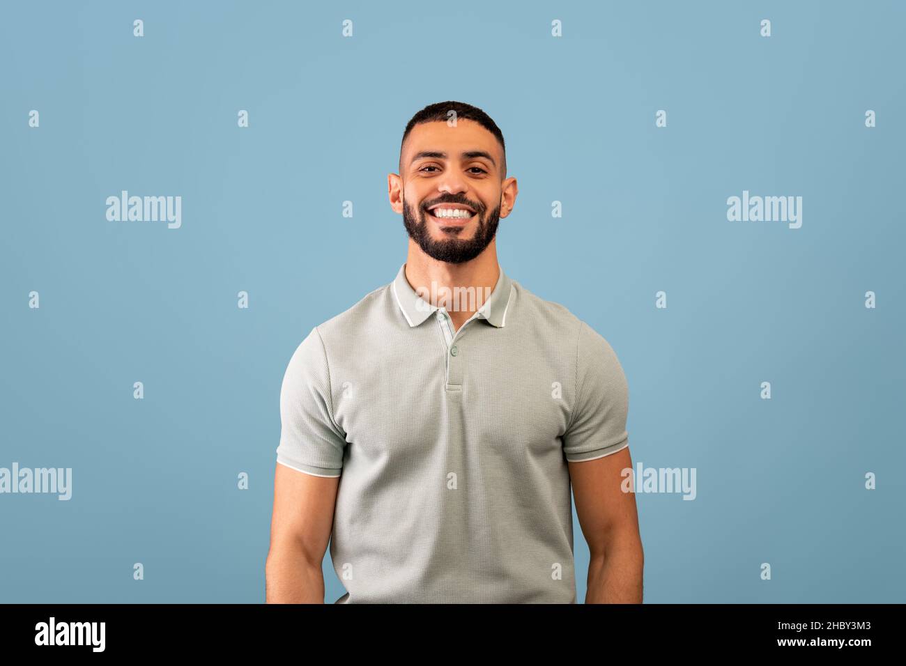 Portrait of happy arabic guy smiling at camera over blue studio ...