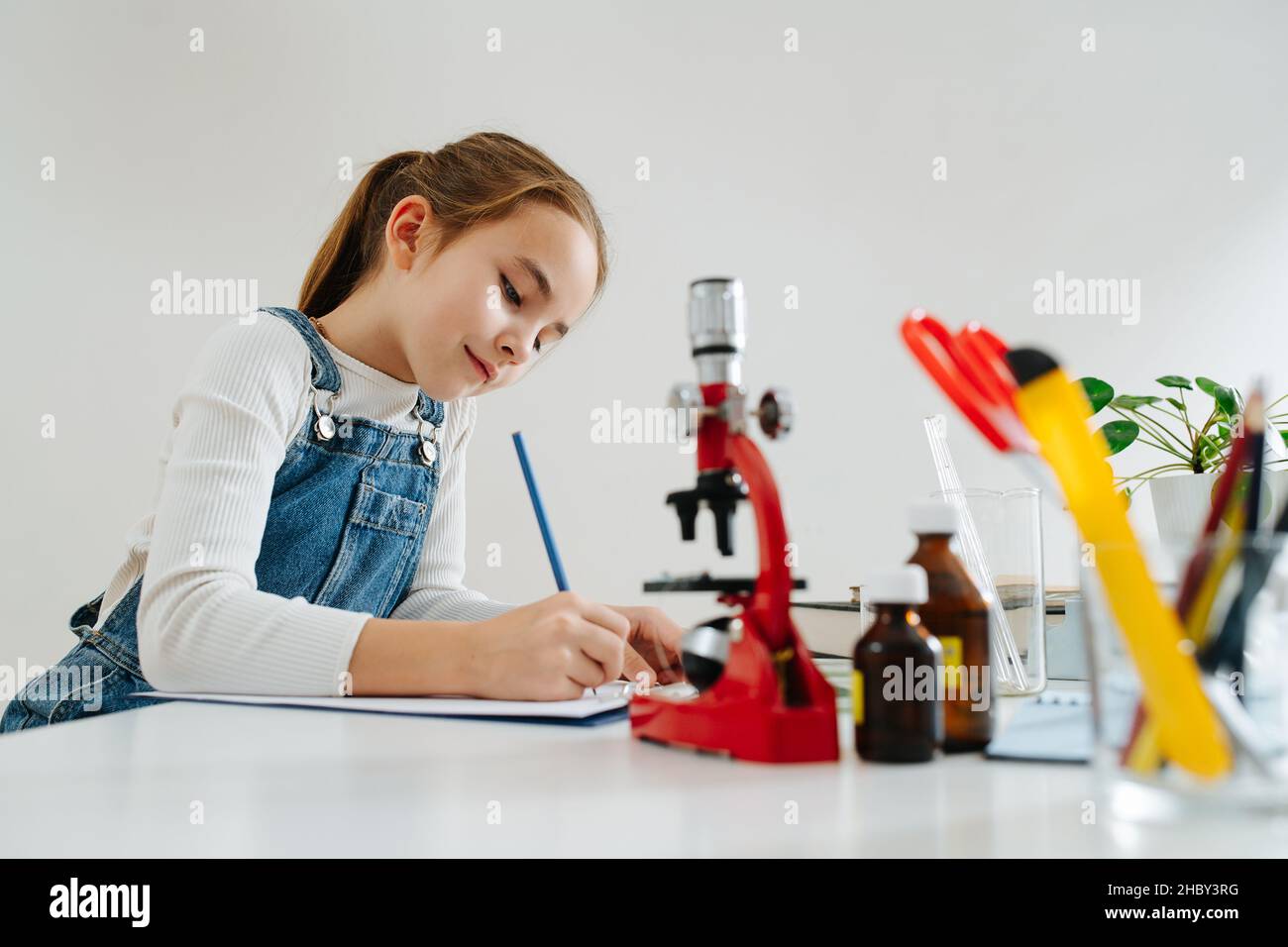 Diligent little girl trying to do home science project, writing dow her ...
