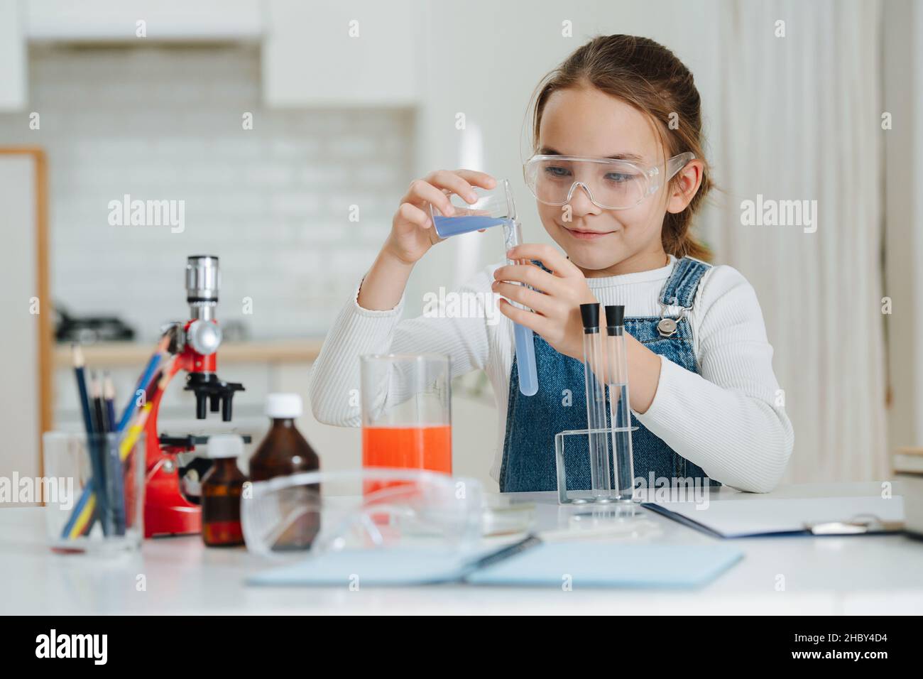 Smug little girl doing home science project, pouring blue liquid into a ...