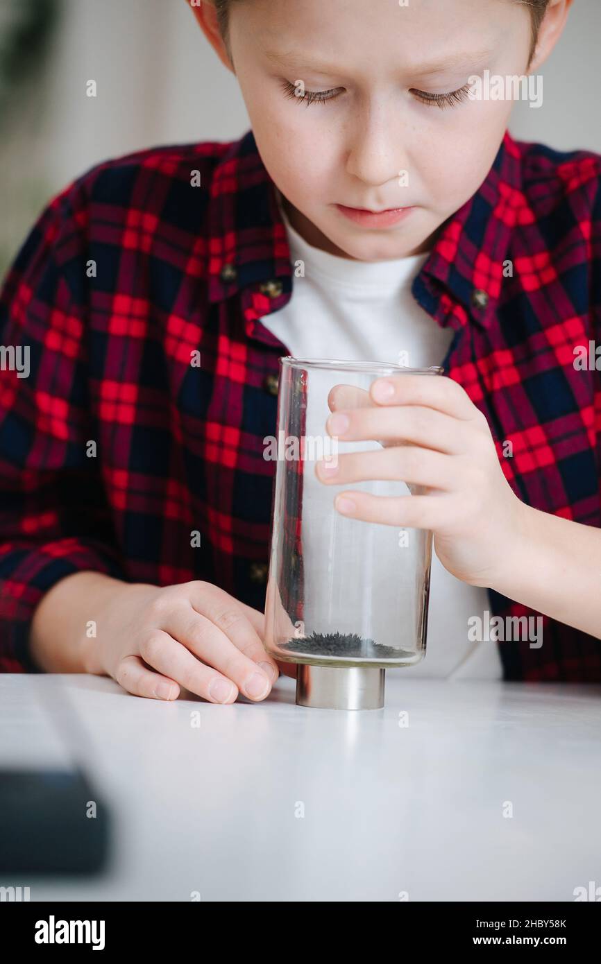 Little boy doing science project, looking at iron filings alligned with ...