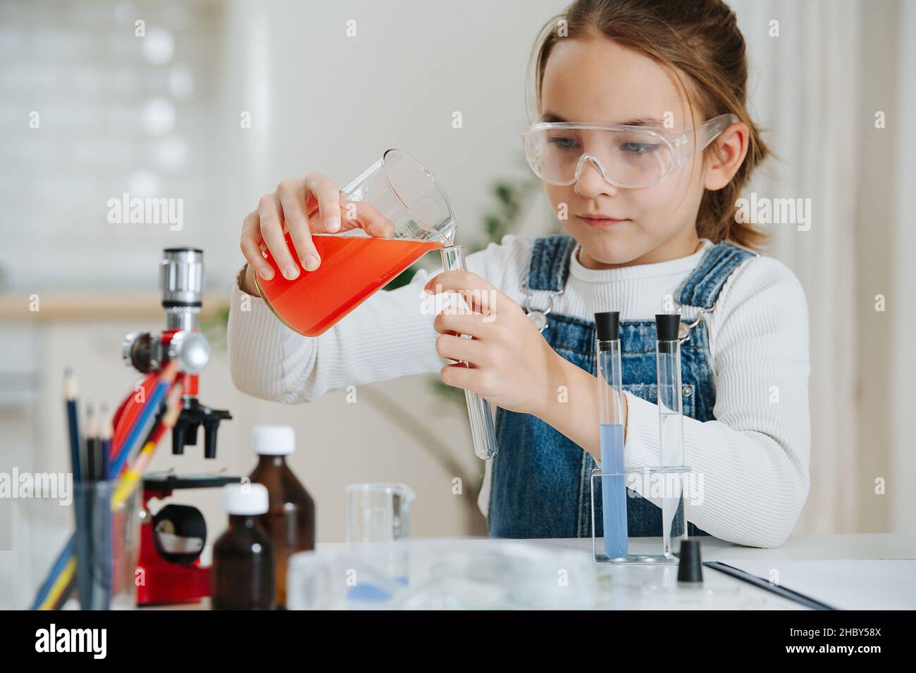 Calm little girl doing home science project, pouring red liquid into a ...