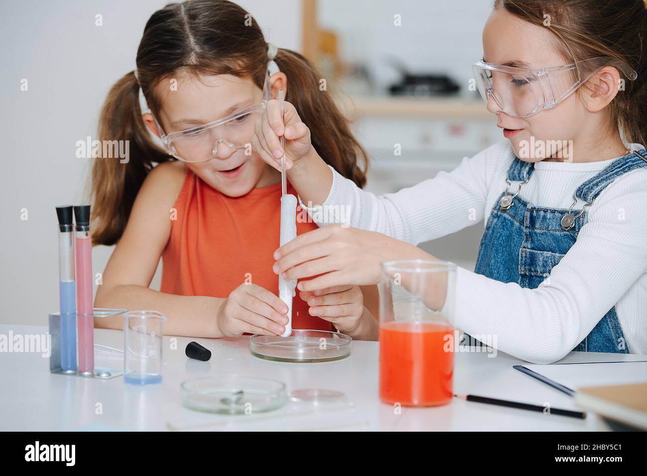 Amased little girls doing science project, one is adding liquid into a ...