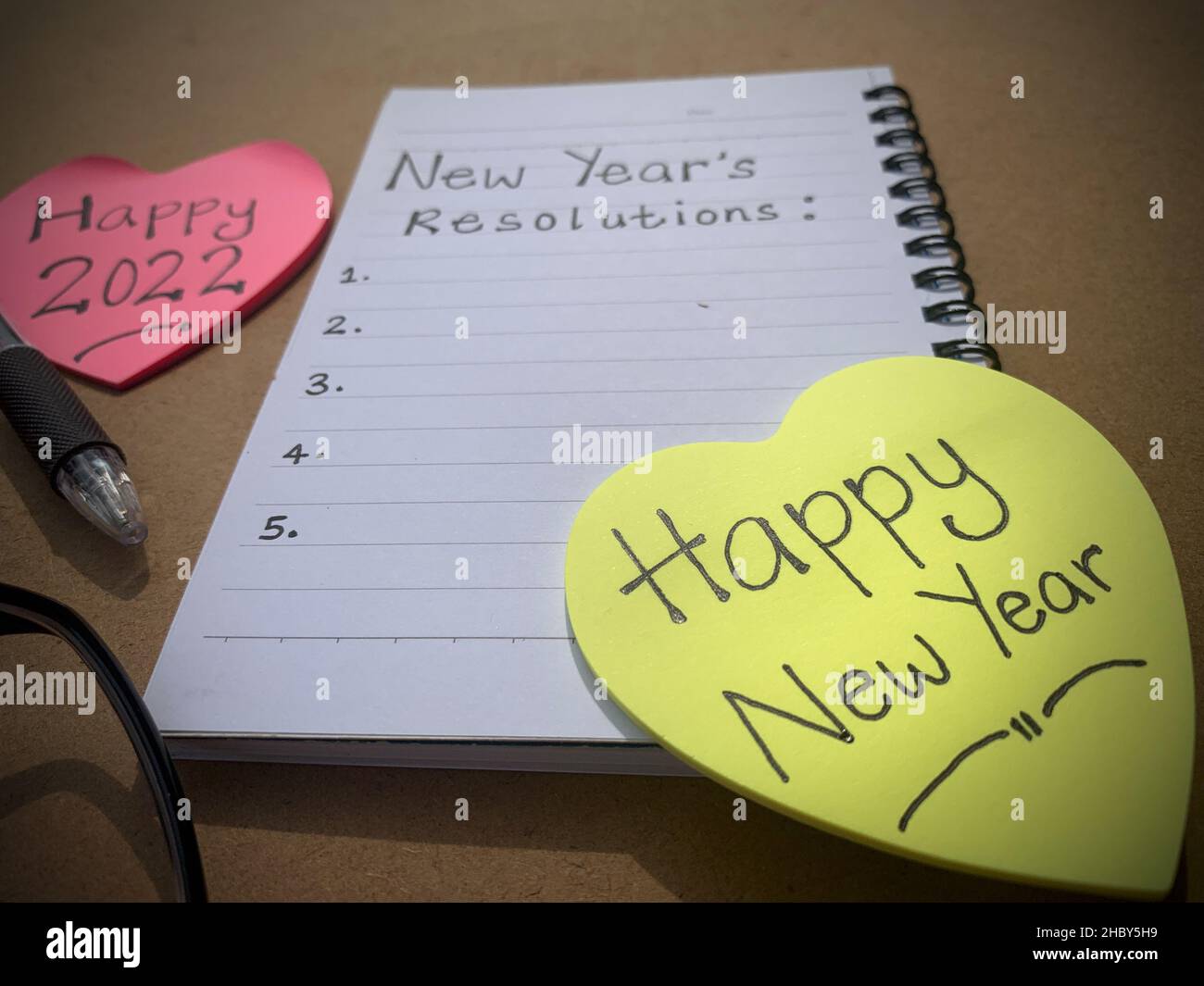 Wishing happy new year on a stick note with a hearth shape with notepad ...