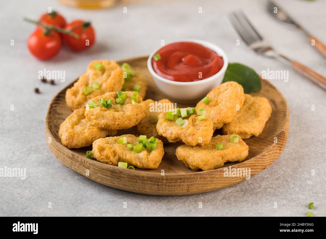 Golden chicken nuggets in a wooden plate, sprinkled with green onions ...