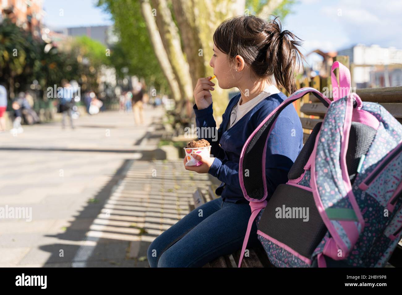 Side view of little girl eating ice cream sitting on park bench by ...