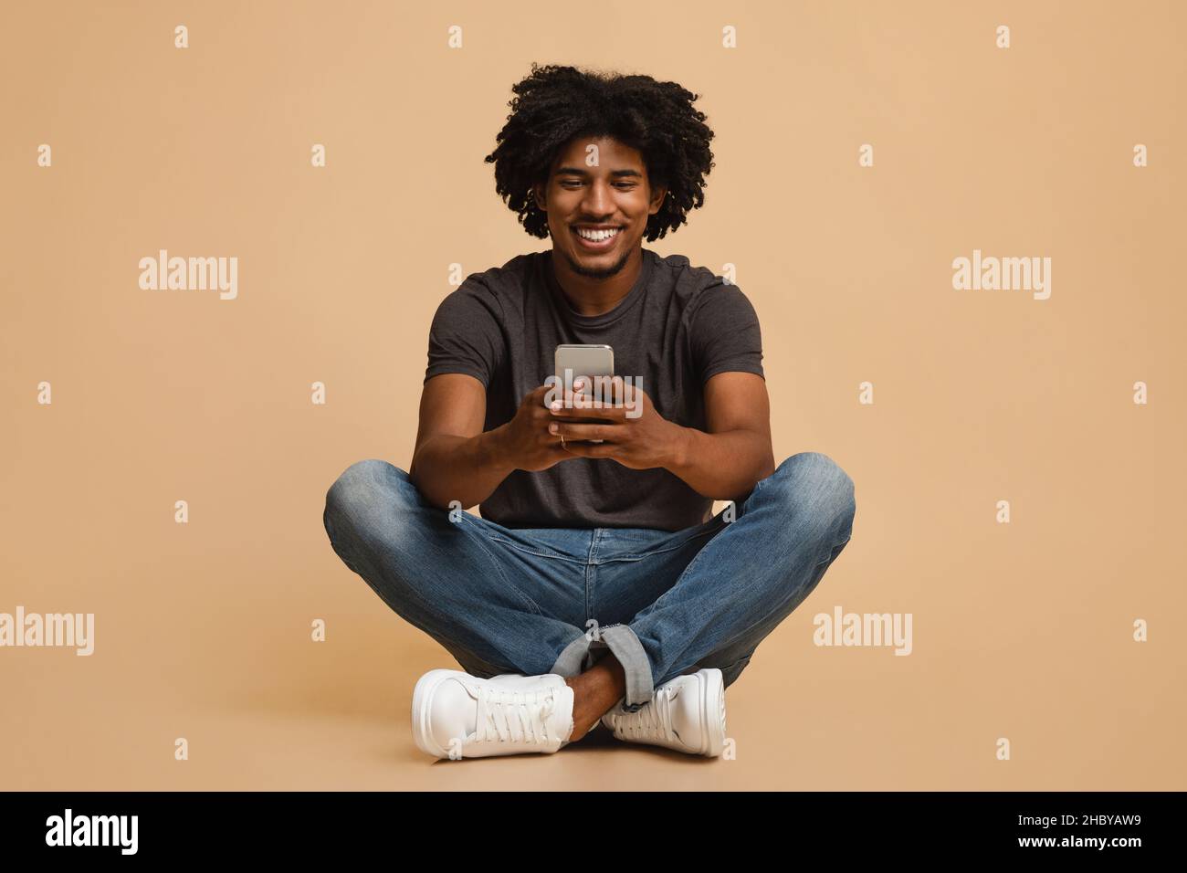 Happy Millennial African American Guy Using Smartphone Sitting Over