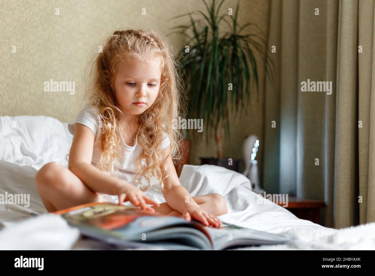 Beautiful little child calm Attentive Child read book on bed. Little ...