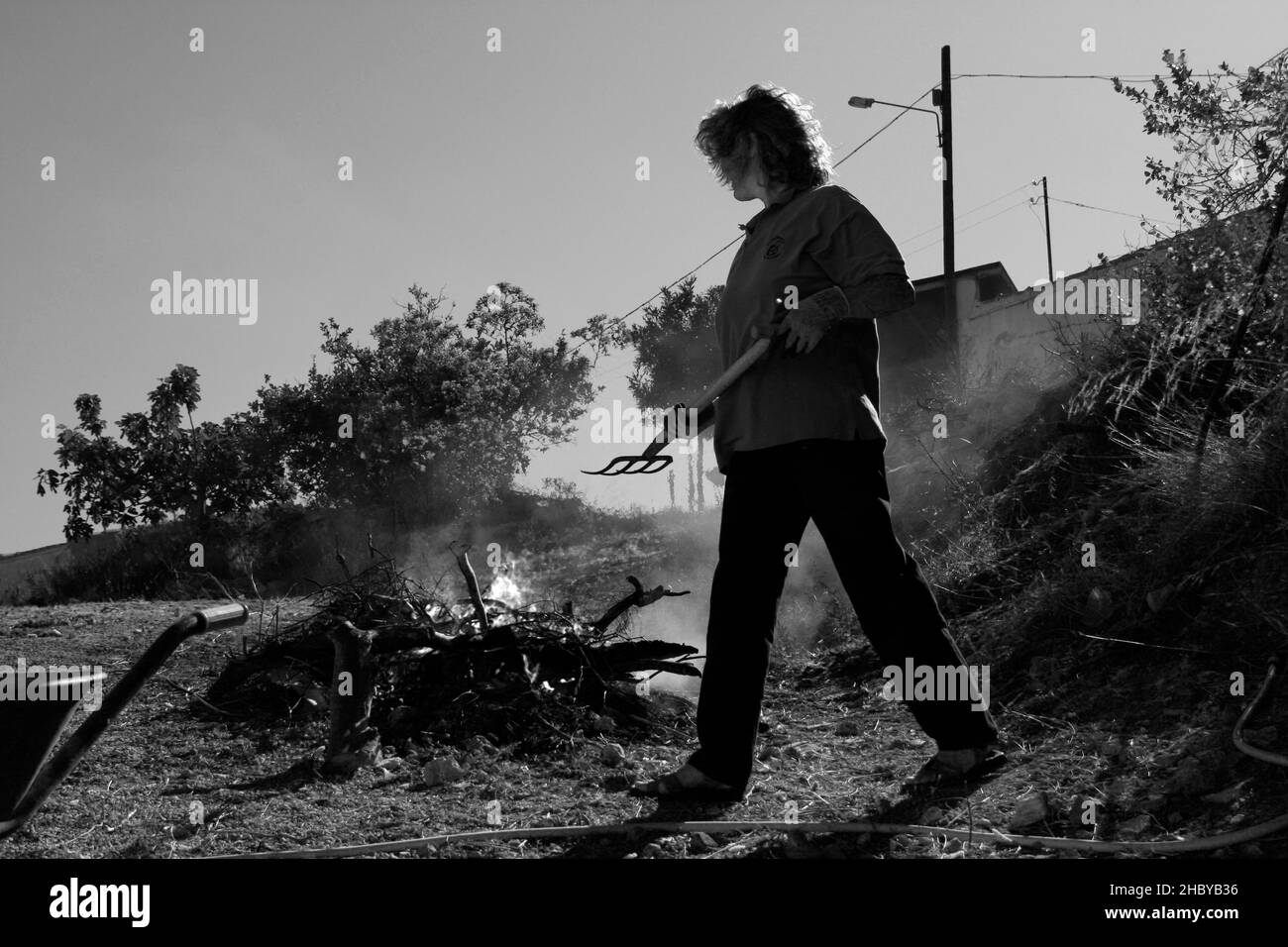 Woman with pitchfork in front of fire with garden waste, burning wood ...