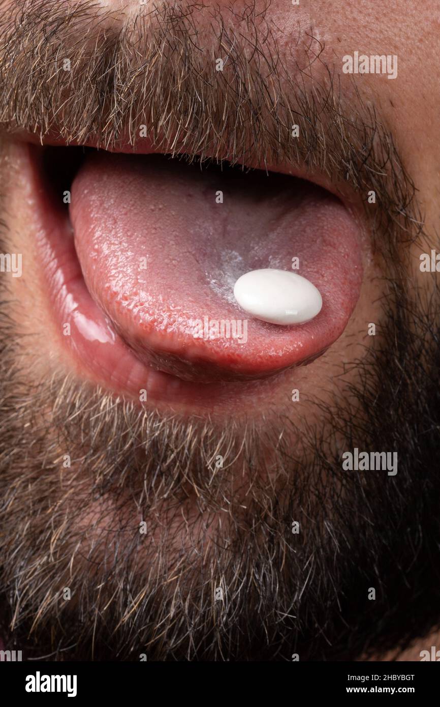Extreme close up of white round pill on tongue of bearded man face with ...